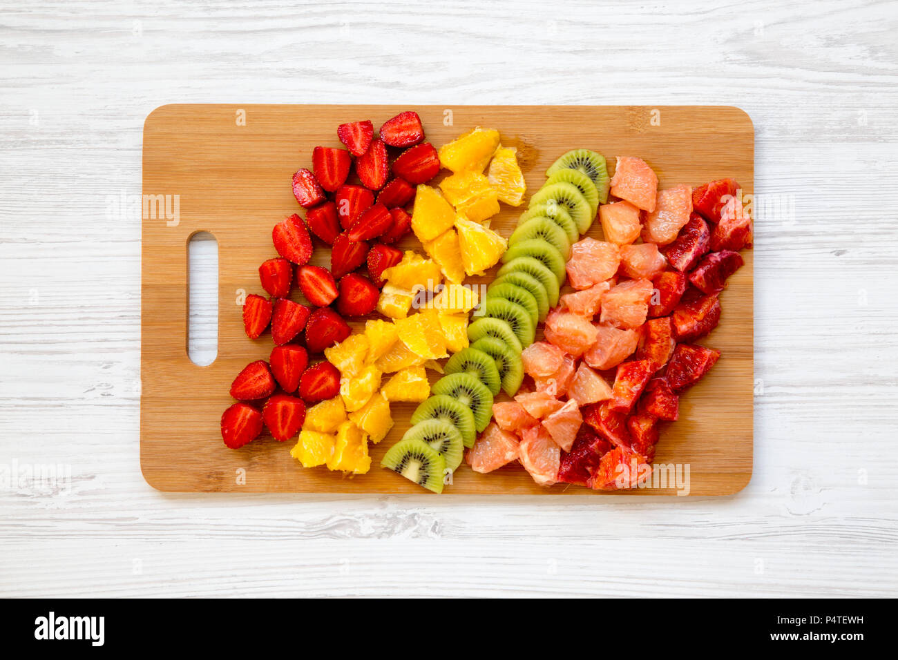 Chopped fresh raw fruits arranged on cutting board on white wooden ...