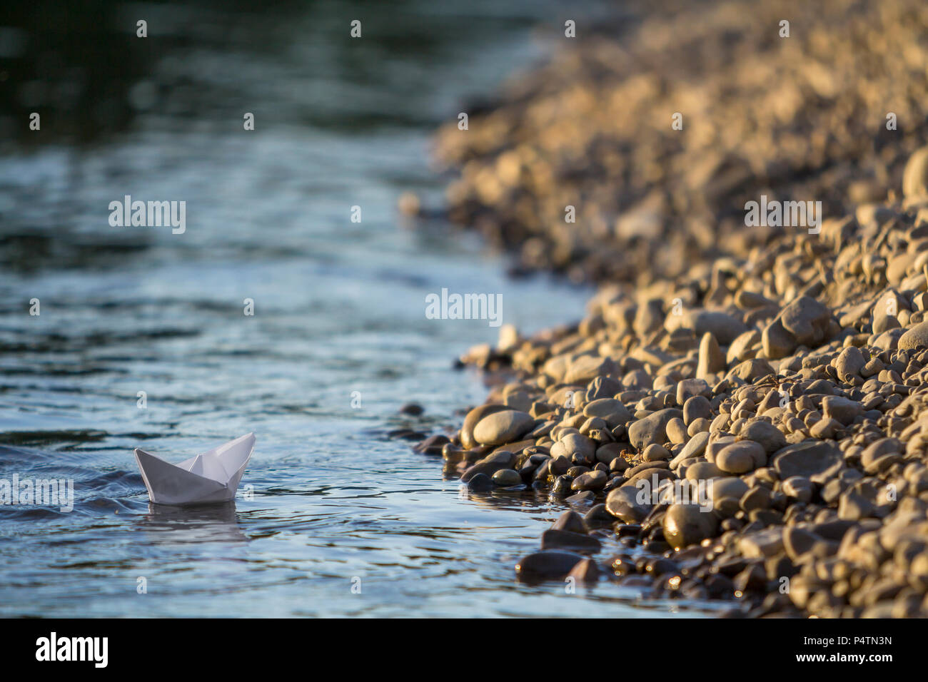 Simple small white origami paper toy boat floating in clear river or ...