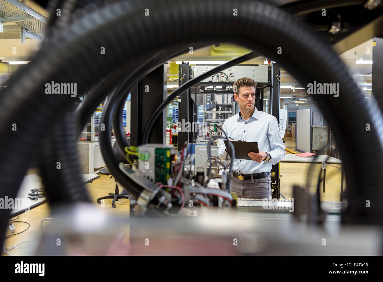Man with clipboard in factory looking around Stock Photo - Alamy