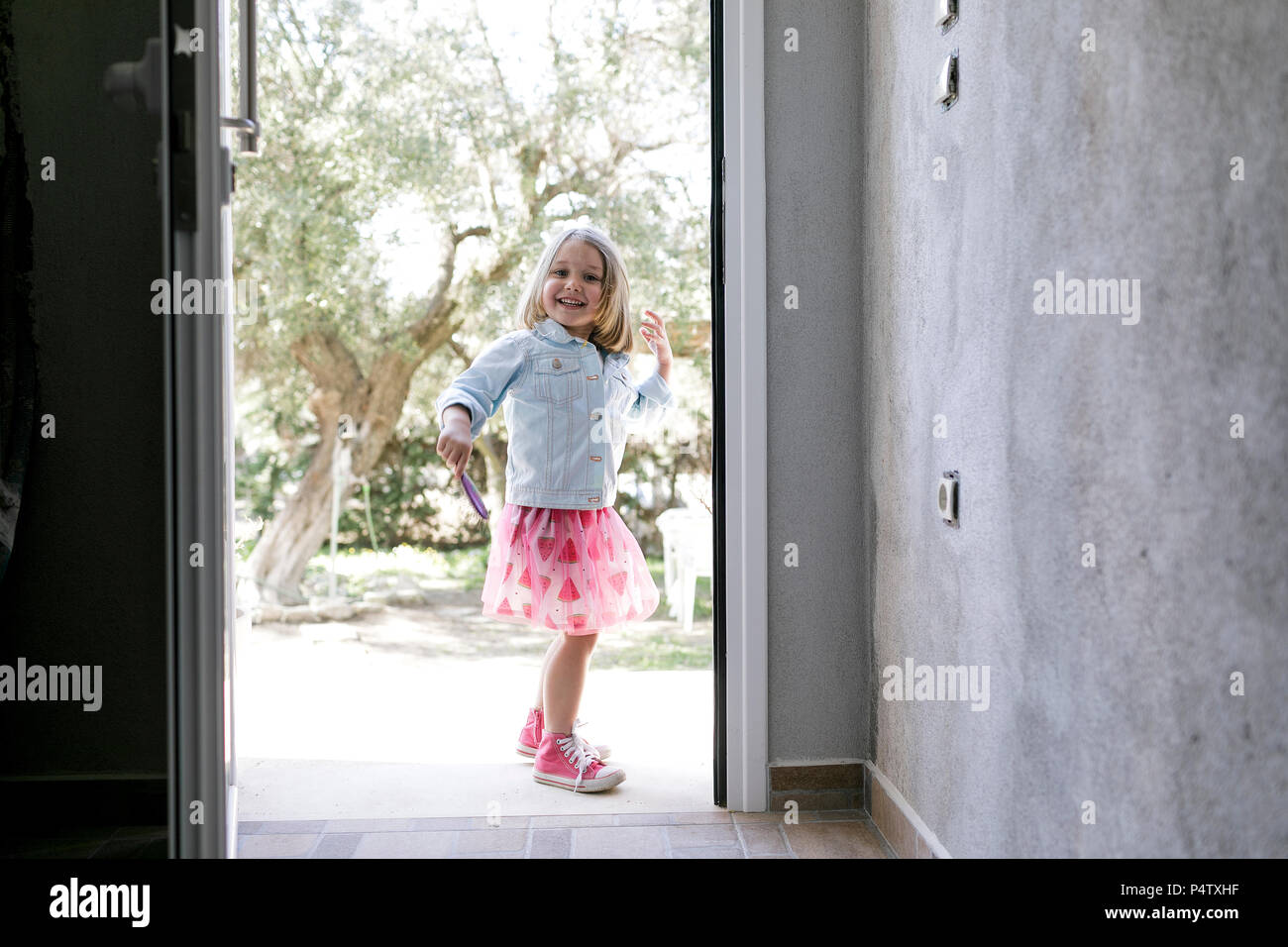 Portrait of laughing little girl standing in front of open entry door ...