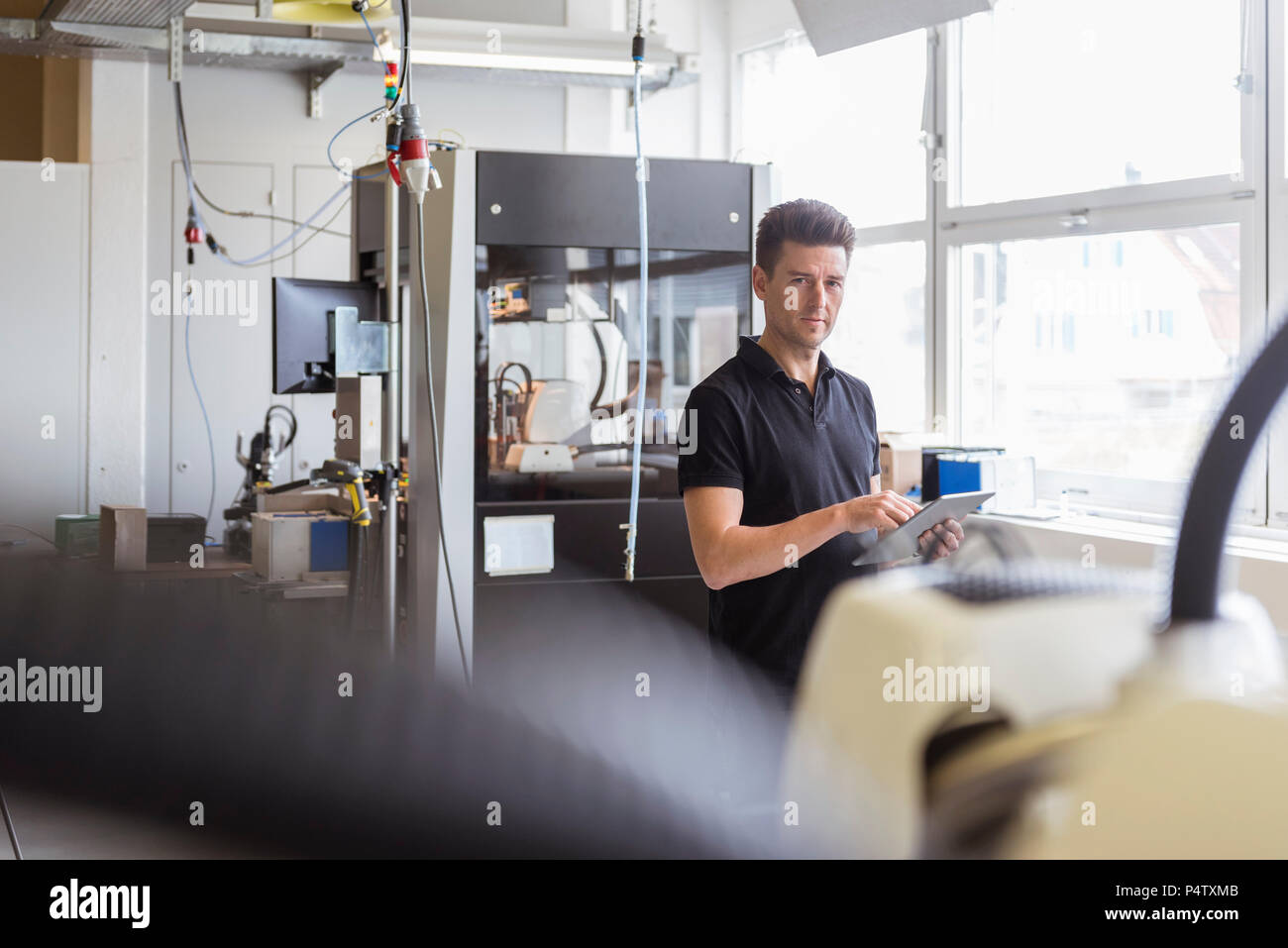 Man standing in factory with tablet looking at machine Stock Photo - Alamy
