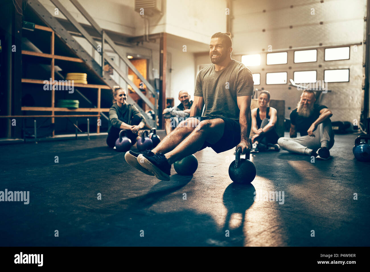 Fit young man working out with dumbbells with friends watching in the ...