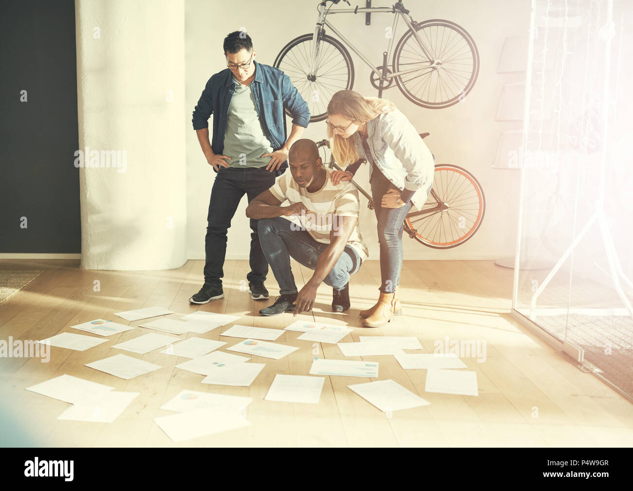 Three diverse colleagues standing in cool modern office going over ...