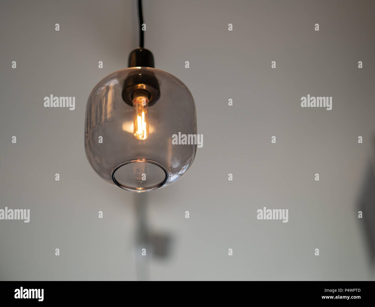 Stylish incandescent lightbulb enclosed in glass hanging from ceiling ...