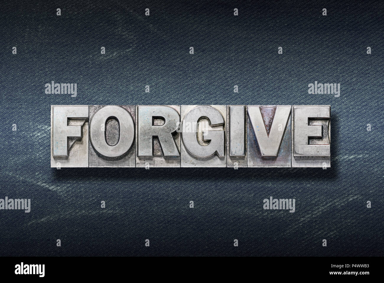 forgive word made from metallic letterpress on dark jeans background ...