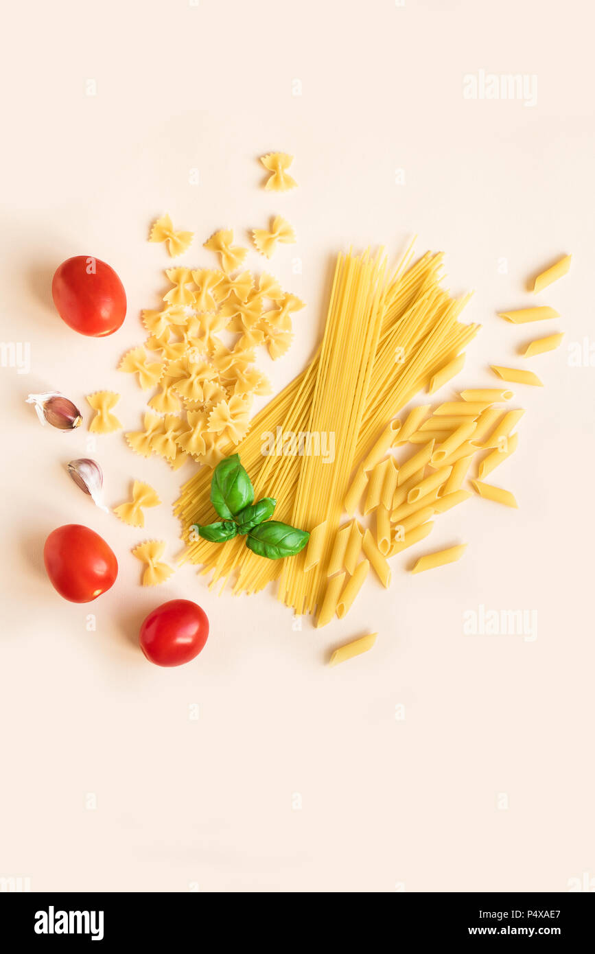 Various uncooked raw pasta with basil,tomatoes and garlic on pink ...