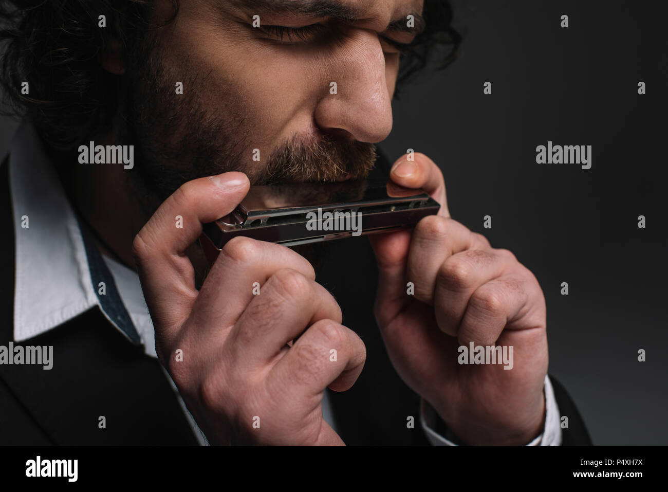 close-up portrait of expressive musician playing harmonica on black ...