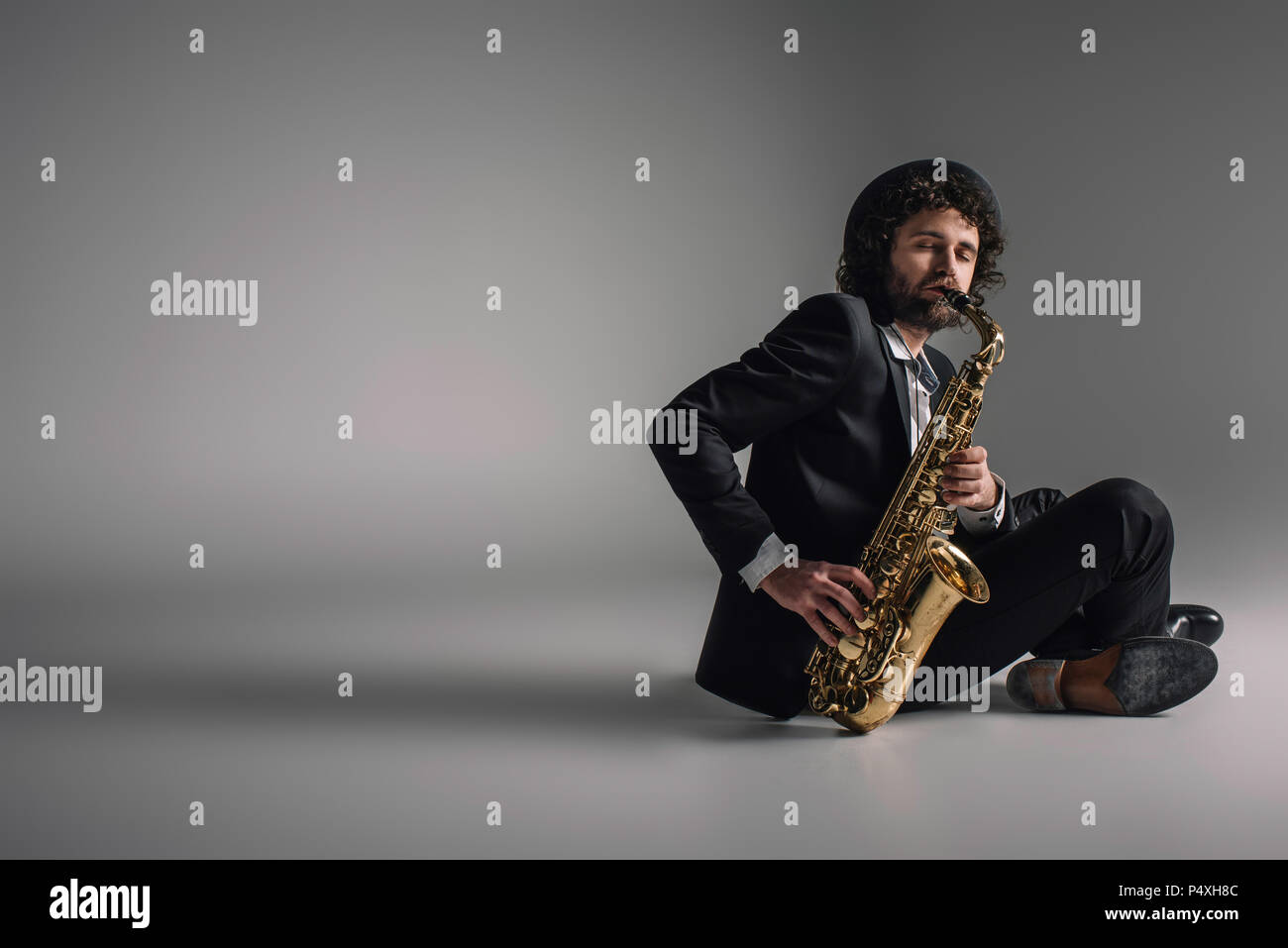 stylish musician playing saxophone while sitting on floor Stock Photo ...