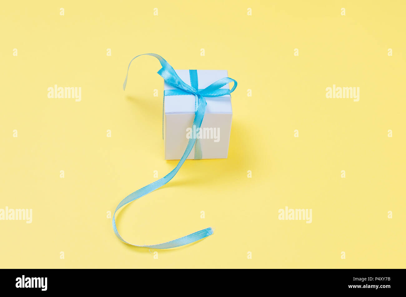 white gift box with blue ribbon over the light yellow background Stock ...