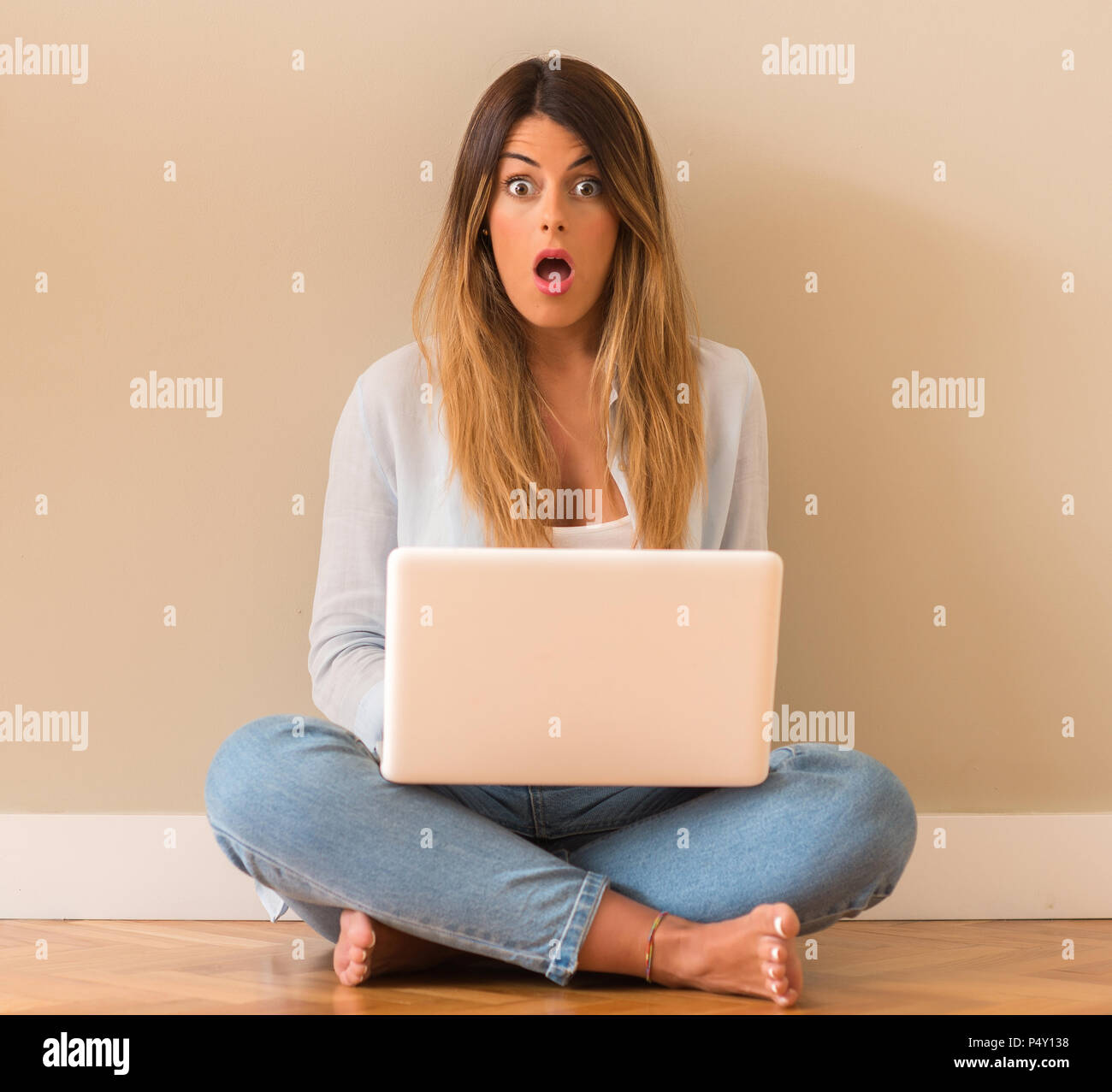 Young beautiful woman suprised sitting on the floor with computer ...