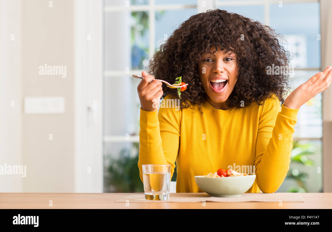 African american woman eating pasta salad at home very happy and ...