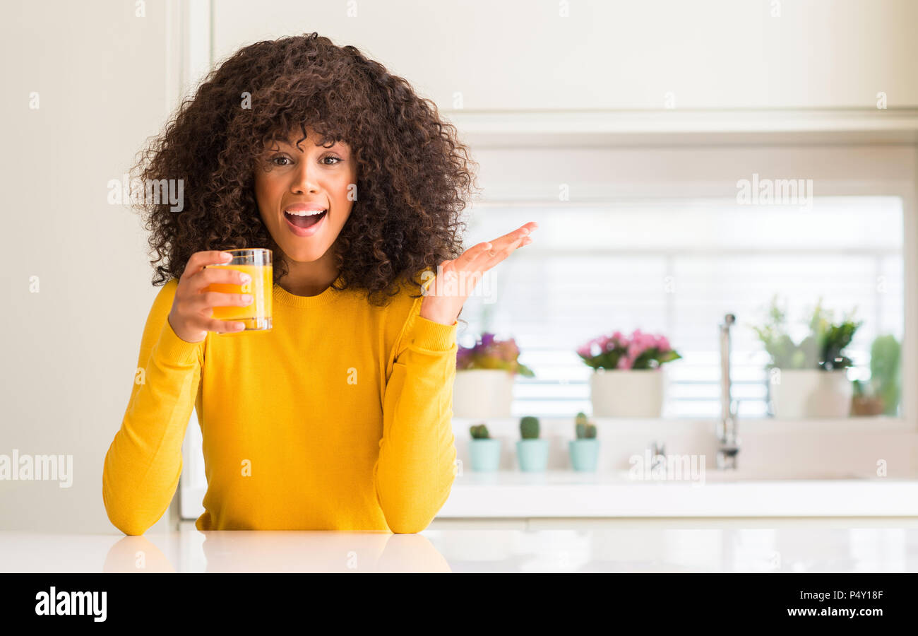 African american woman drinking orange juice in a glass very happy and ...