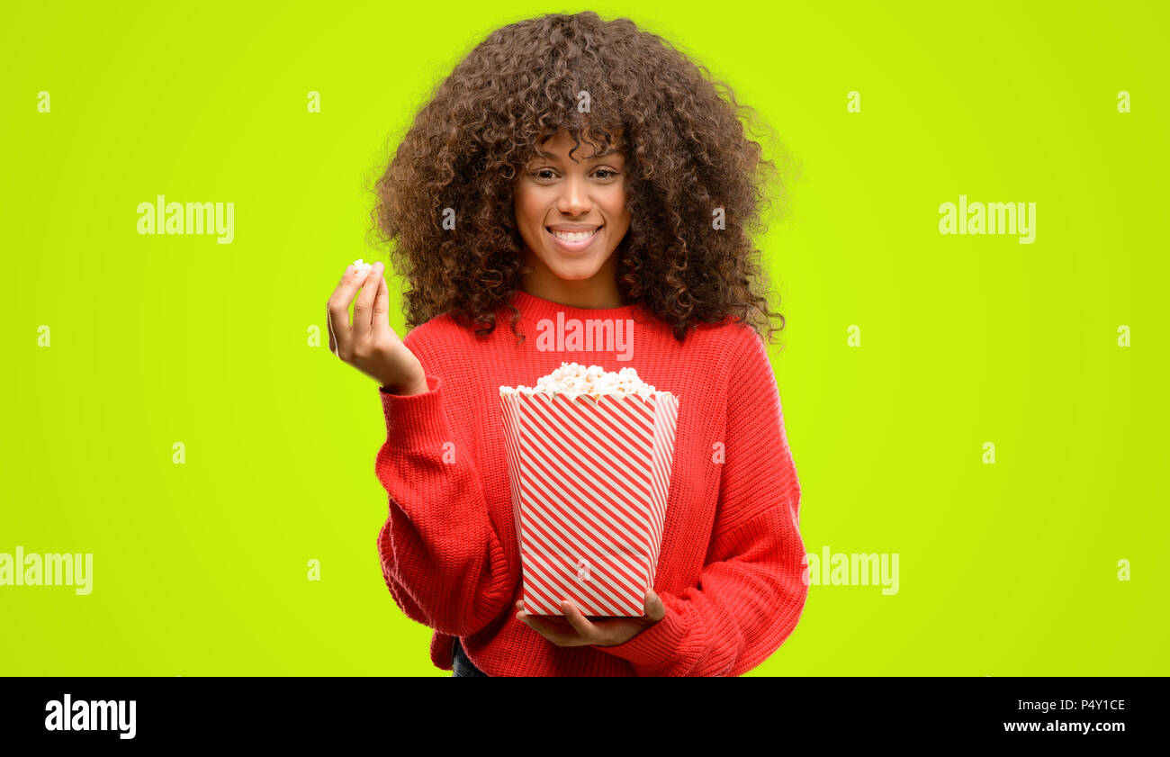 African american woman eating popcorn with a happy face standing and ...