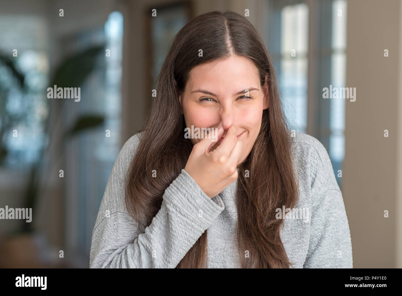 Young beautiful woman at home smelling something stinky and disgusting ...