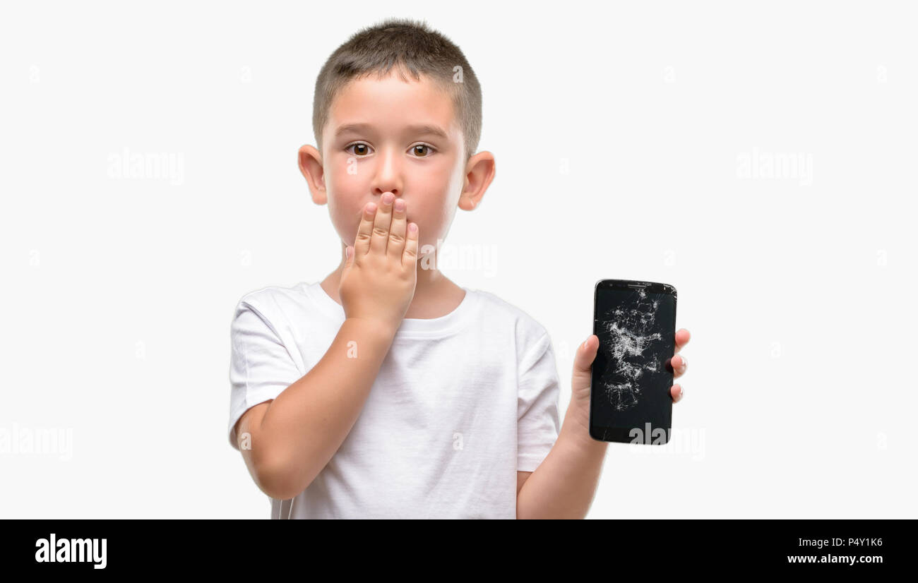 Dark haired little child holding broken smartphone cover mouth with ...
