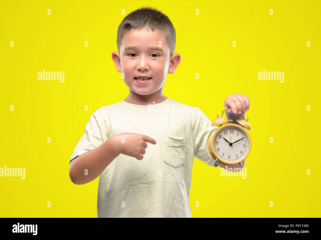 Little child holding alarm clock very happy pointing with hand and ...