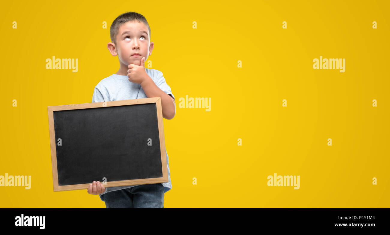 Dark haired little child holding a blackboard serious face thinking ...
