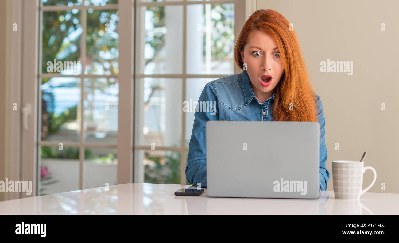 Redhead woman using computer laptop at home scared in shock with a ...