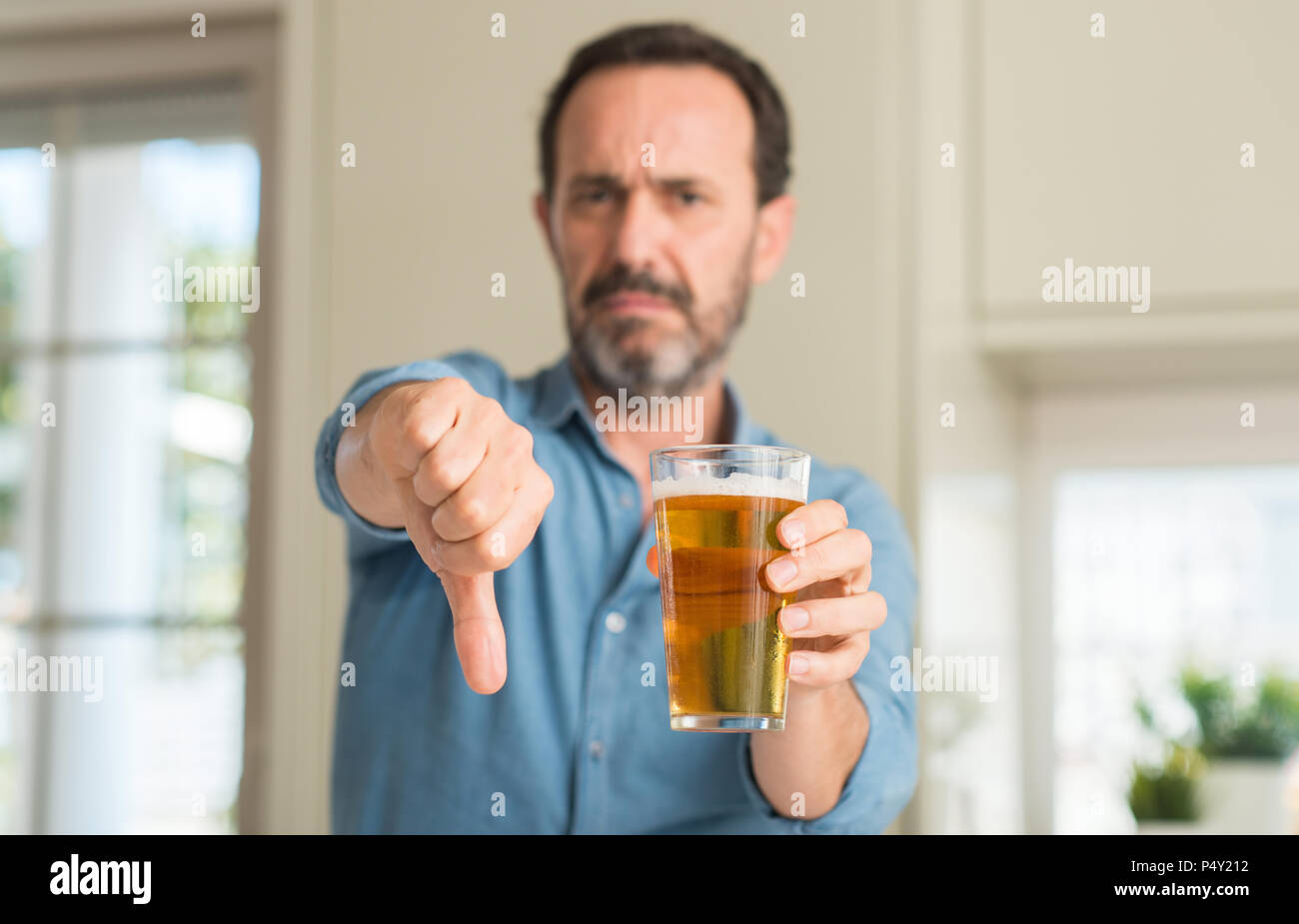 Middle age man drinking beer with angry face, negative sign showing ...