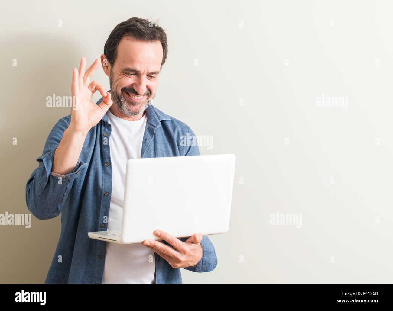 Senior man using laptop computer doing ok sign with fingers, excellent ...