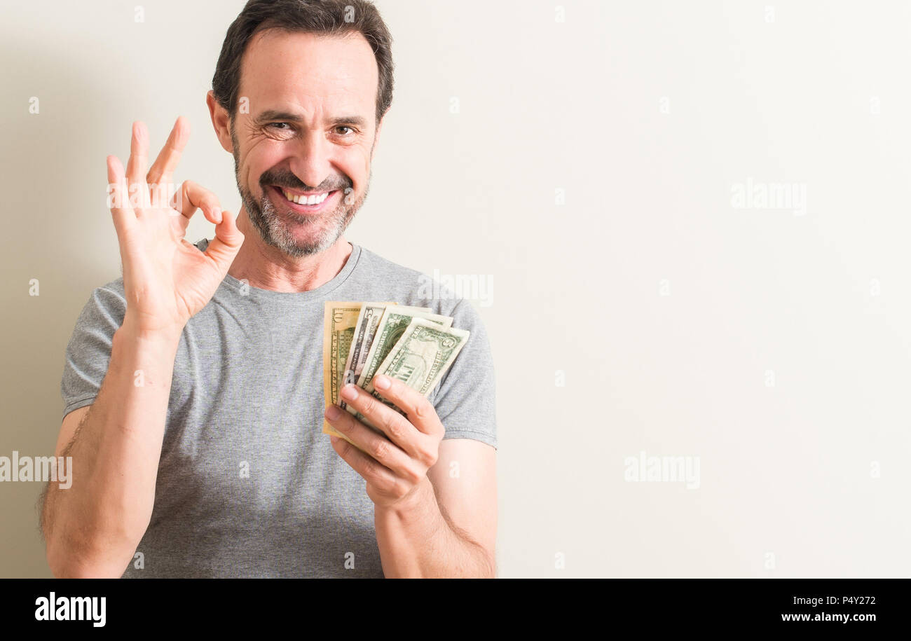 Senior man holding dollar money doing ok sign with fingers, excellent ...