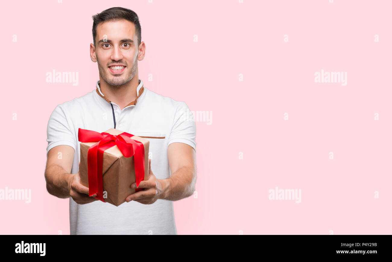 Handsome young man giving a present with a happy face standing and ...
