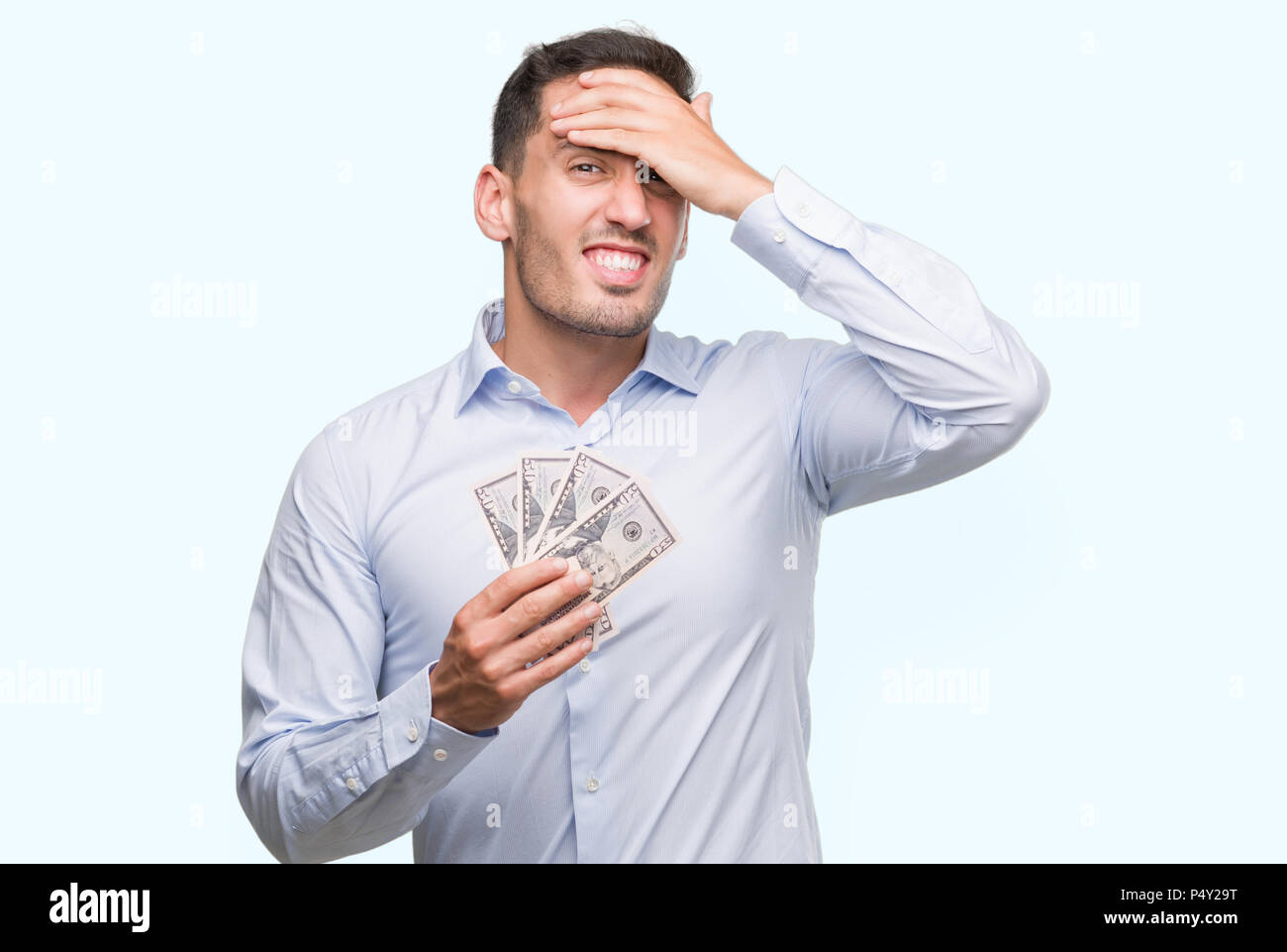 Handsome young man holding money stressed with hand on head, shocked ...