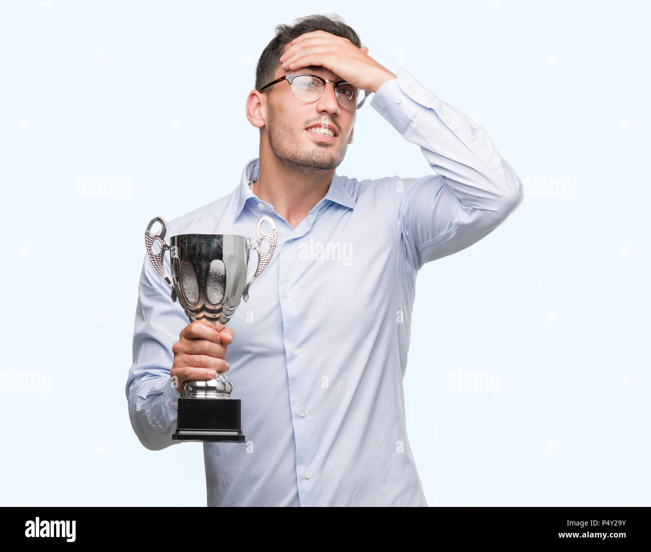 Handsome young man holding trophy stressed with hand on head, shocked ...