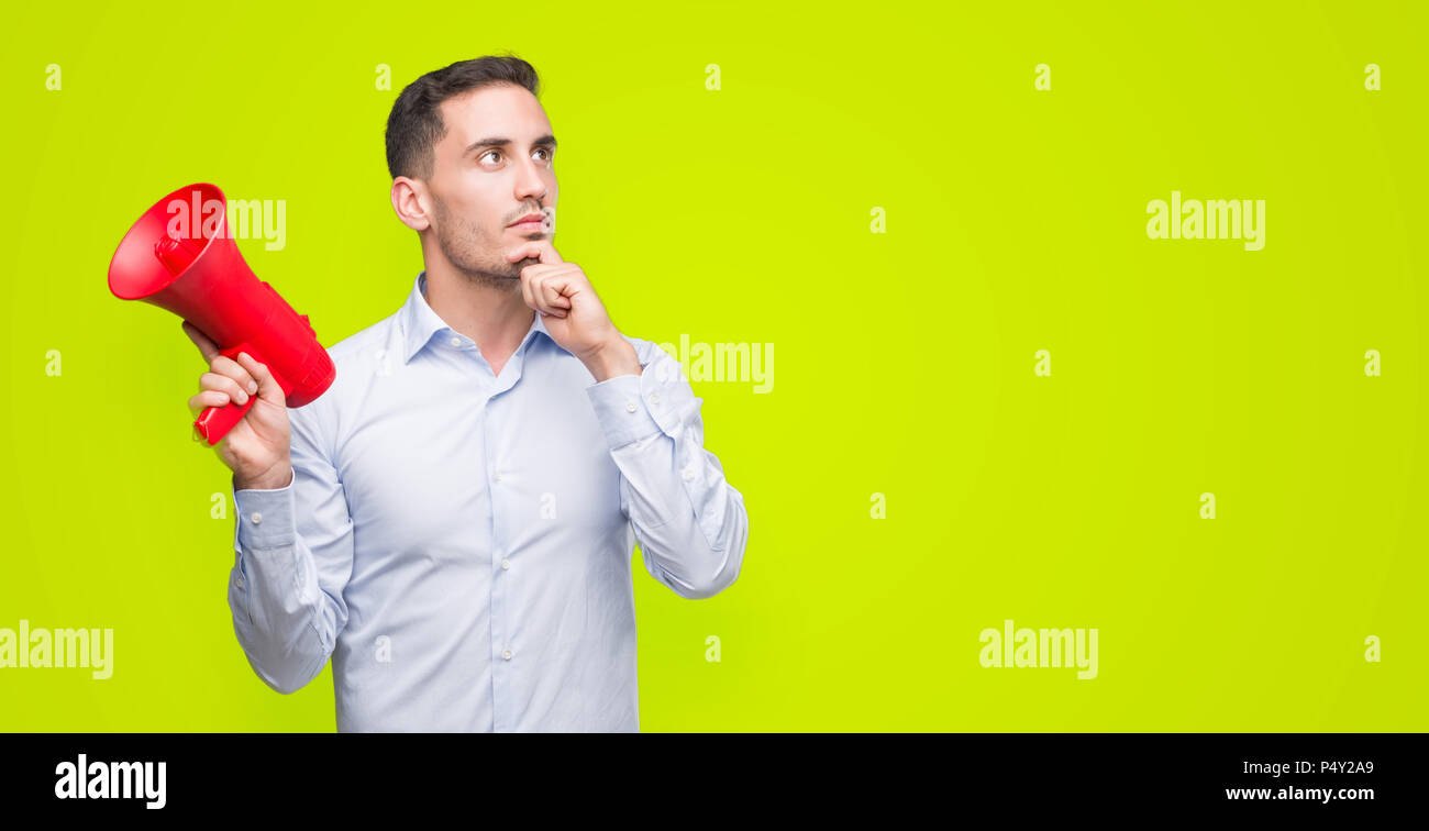 Handsome young man holding microphone serious face thinking about ...