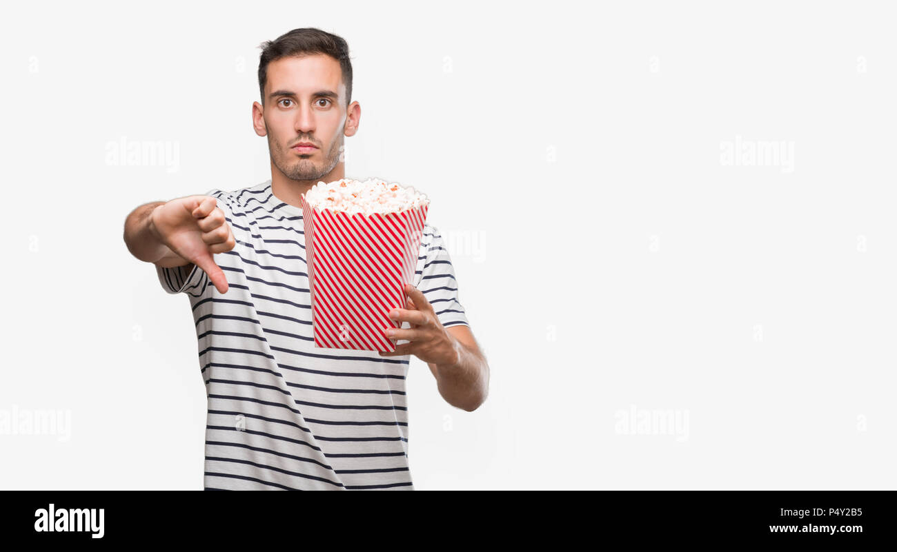 Handsome young man eating popcorn with angry face, negative sign ...