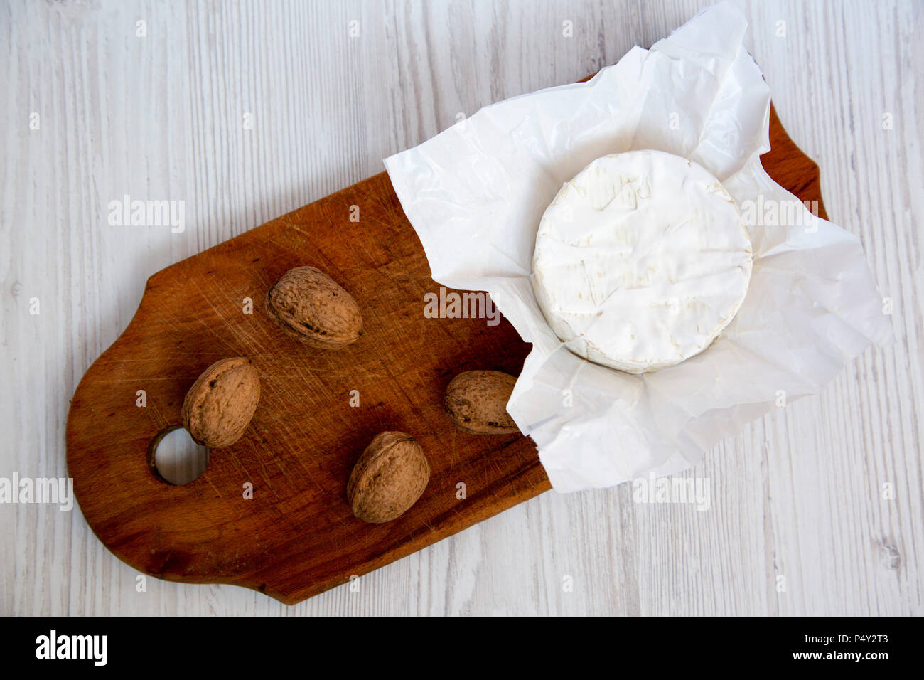 Cheese camembert or brie on dark wooden board with nuts. Light wooden ...