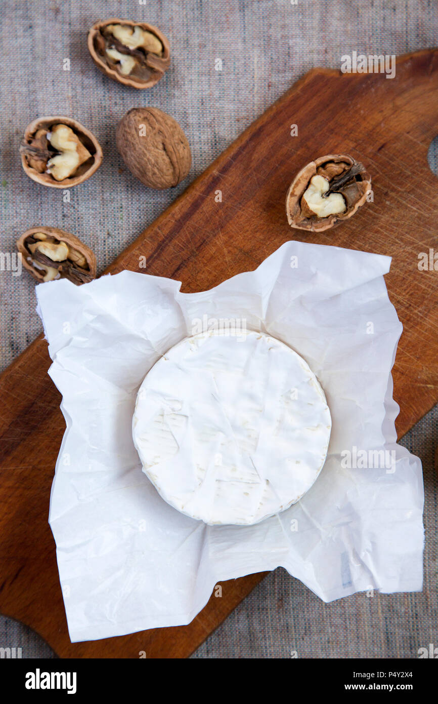 Round Camembert cheese or brie in paper with walnuts on the board. View ...