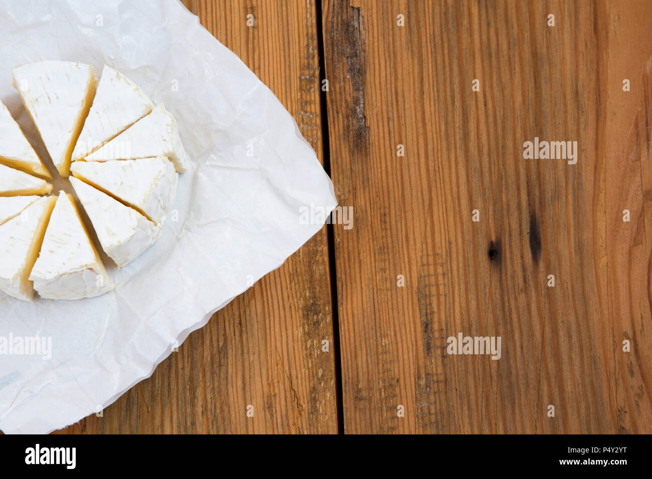 Pieces of round cheese brie or camembert in paper on wooden background ...