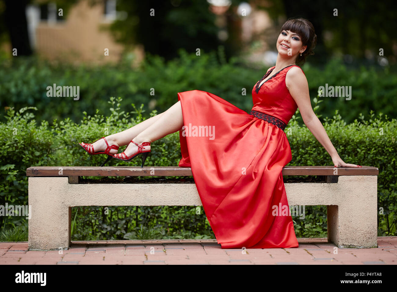 Attractive young girl in red dress sitting on a bench in the park Stock ...