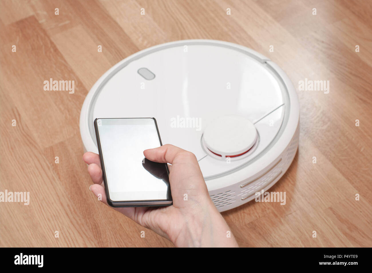 womens hand using mobile to control white robotic vacuum cleaner ...