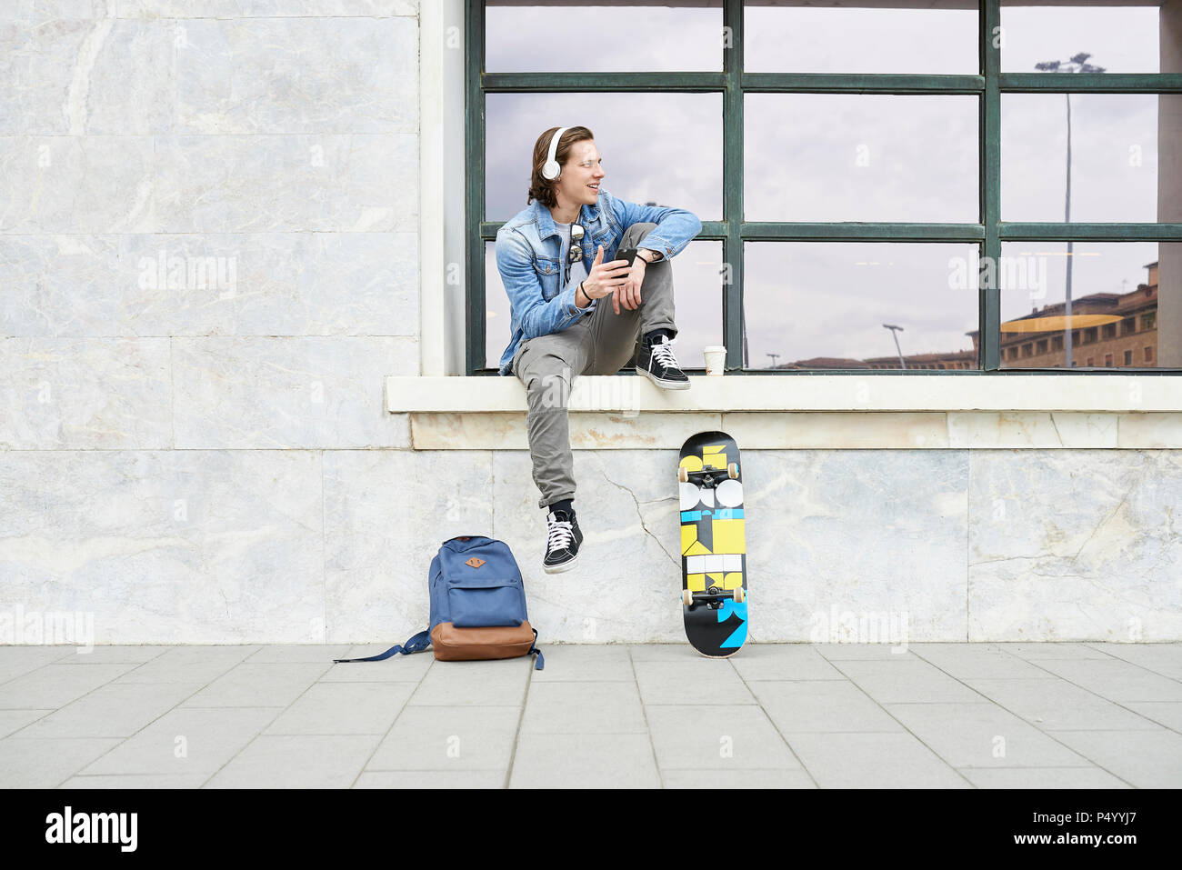 Young man sitting on window sill, waiting, using smartphone Stock Photo ...