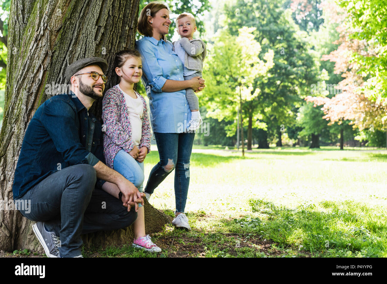 Happy family under a tree in a park Stock Photo - Alamy