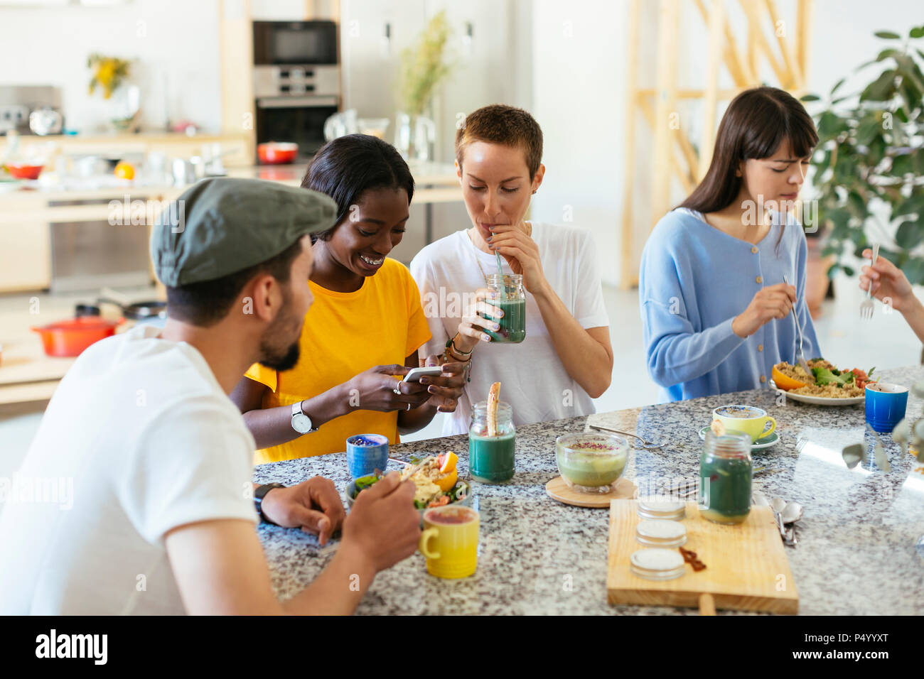 Friends sitting at kitchen counter eating and drinking Stock Photo - Alamy