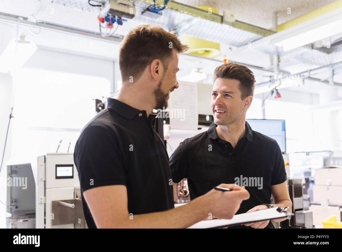 Two men with clipboard talking in factory Stock Photo - Alamy