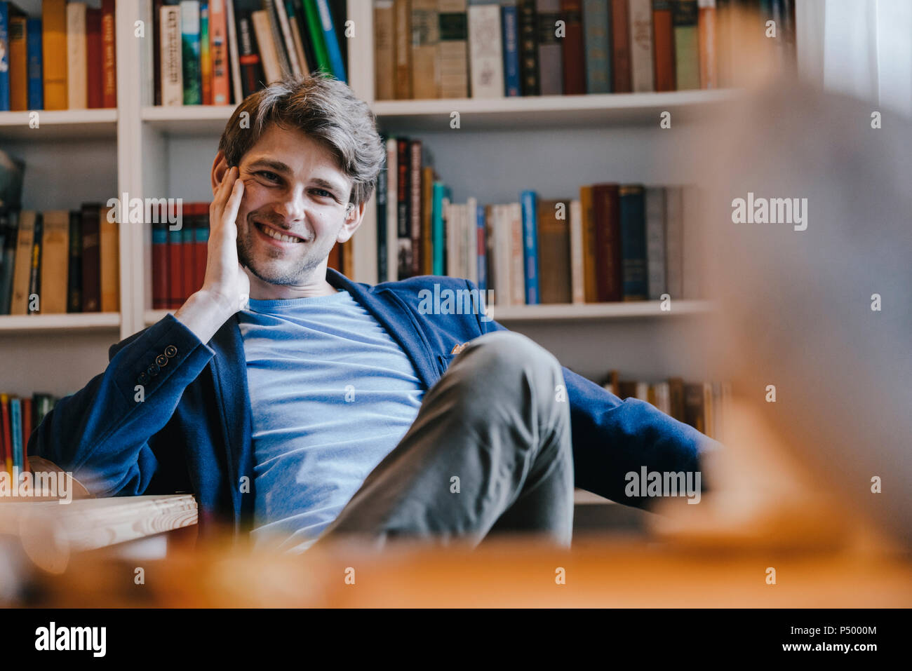 Portrait of smiling man sitting at bookshelf Stock Photo - Alamy