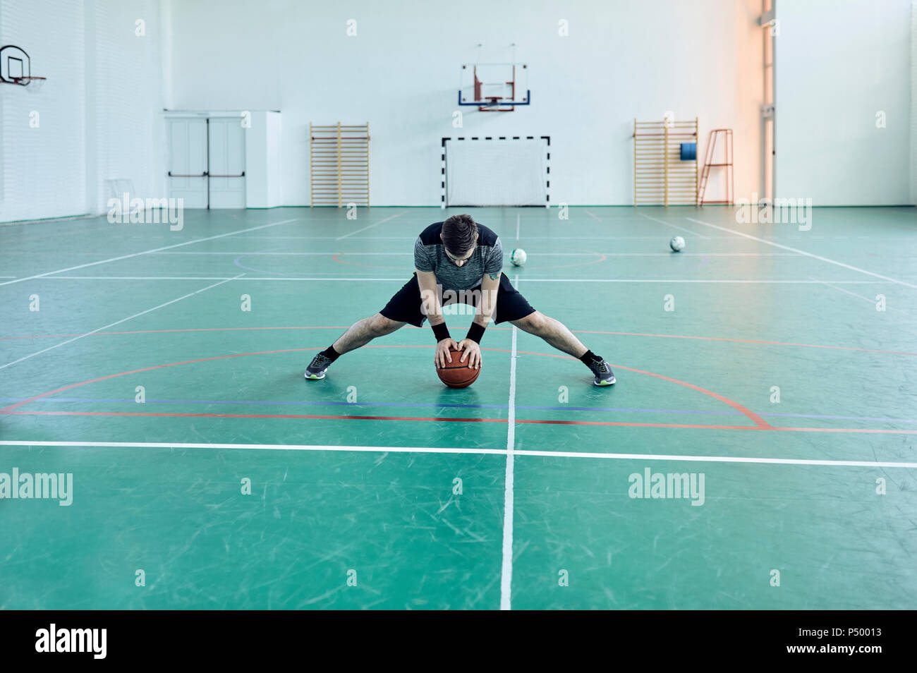 Man with basketball, stretching legs, indoor Stock Photo - Alamy