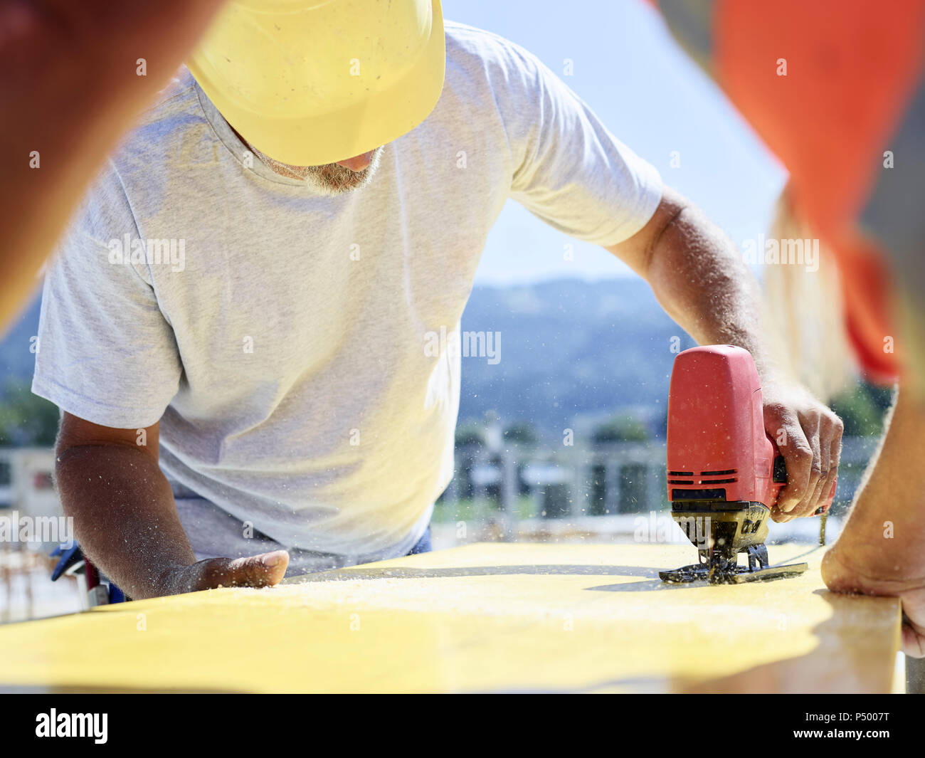 Construction worker cutting plywood with jigsaw on construction site ...