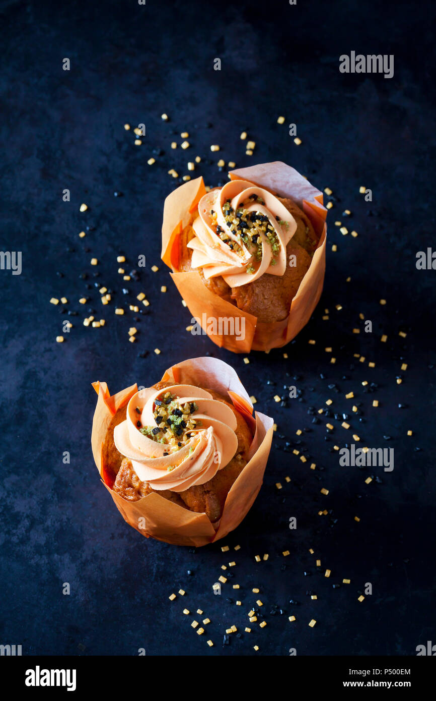 Two carrot cup cakes garnished with cream topping and sugar granules ...