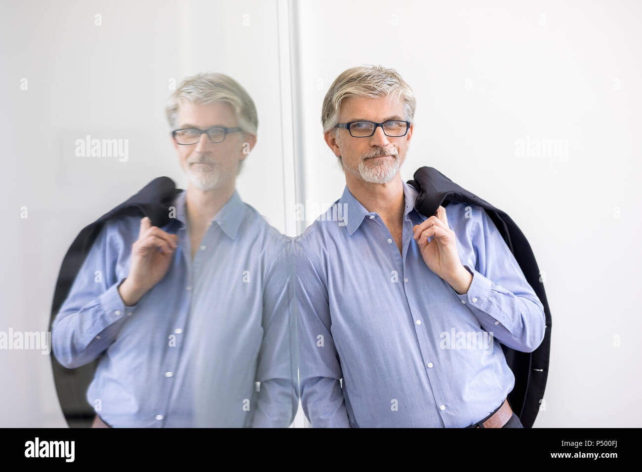 Confident businessman leaning against glass wall hi-res stock ...