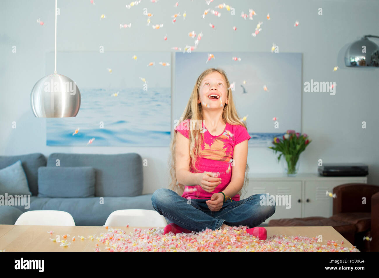 Girl sitting on table, candies falling down Stock Photo - Alamy