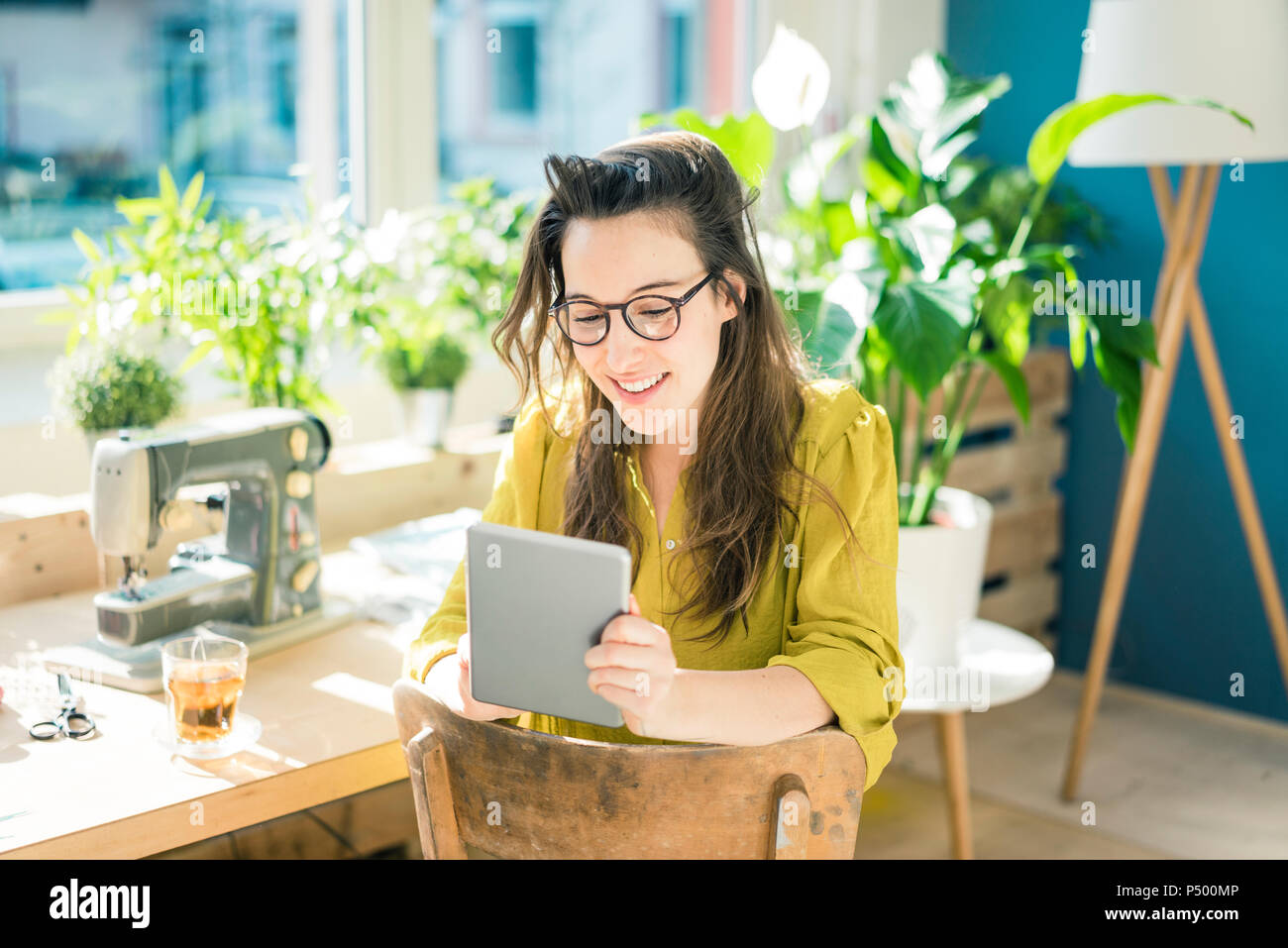 Portrait of smiling fashion designer sitting in her studio using tablet ...
