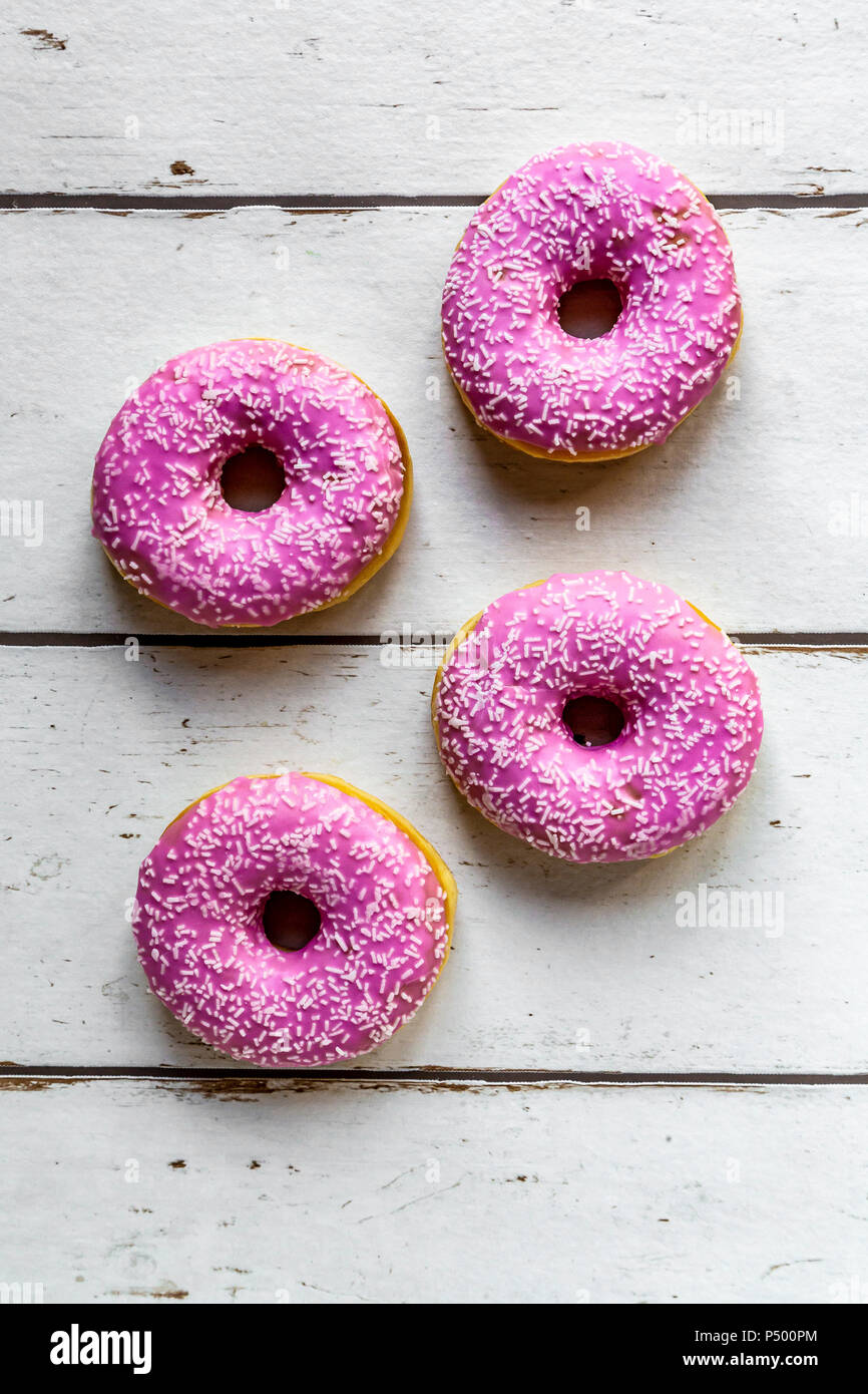 Four pink doughnuts on white wood Stock Photo - Alamy