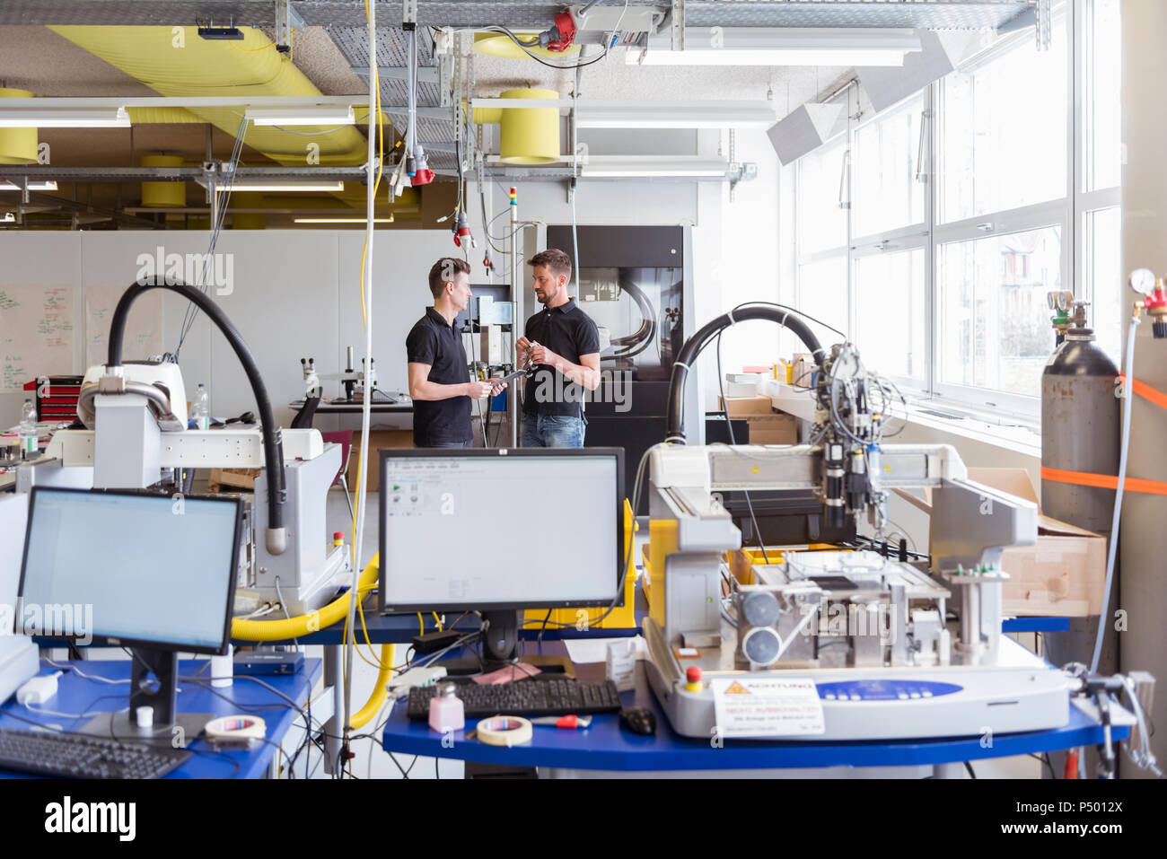Two men talking at machine in factory Stock Photo - Alamy
