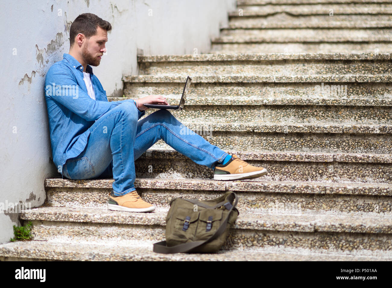 Young man sitting on stairs, working, using laptop Stock Photo - Alamy