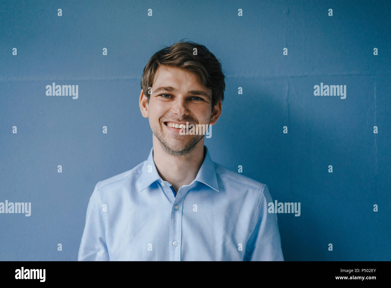 Portrait of smiling man in front of blue wall Stock Photo - Alamy